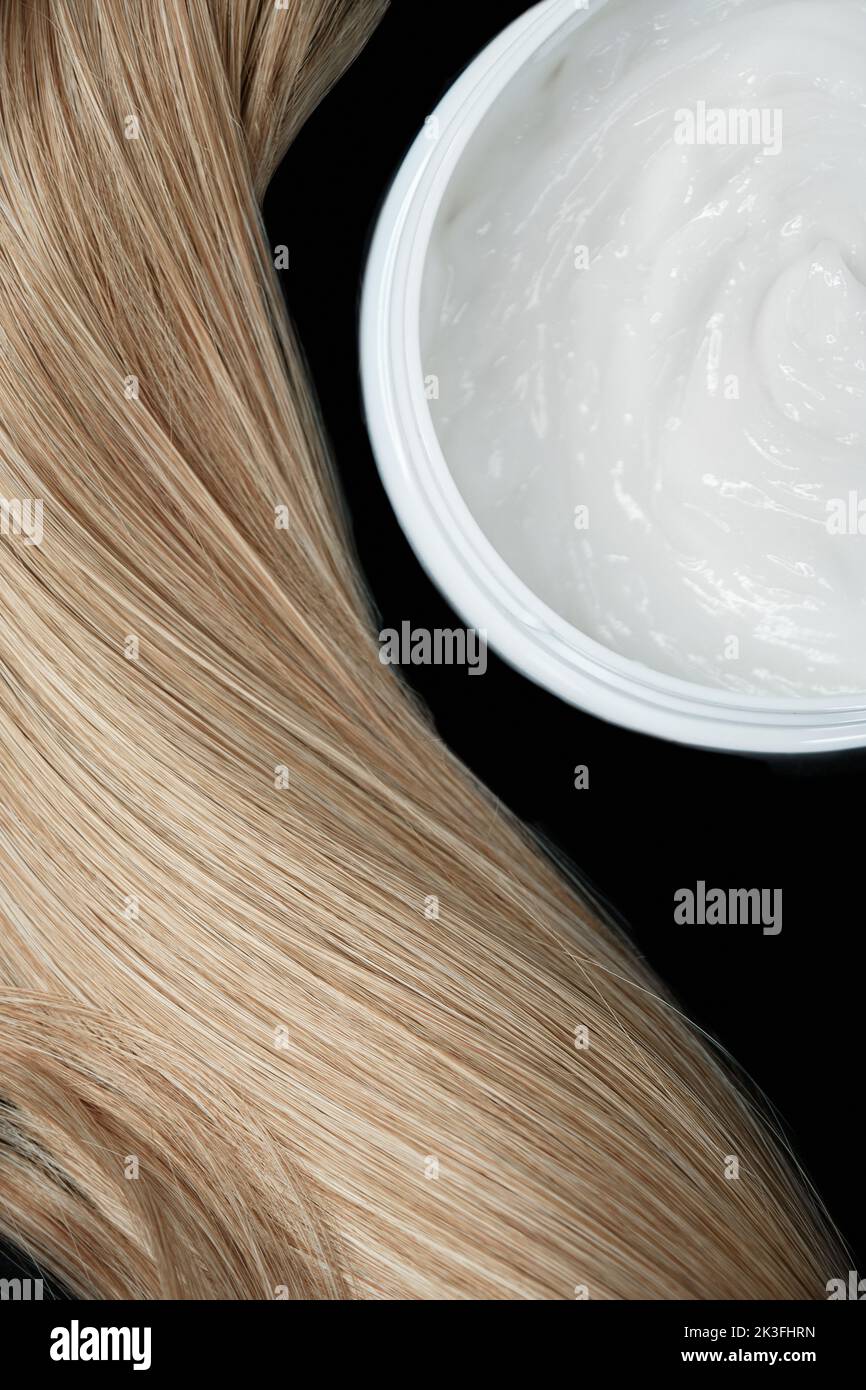 A strand of blond hair with hair balm on a black background. Close-up ...