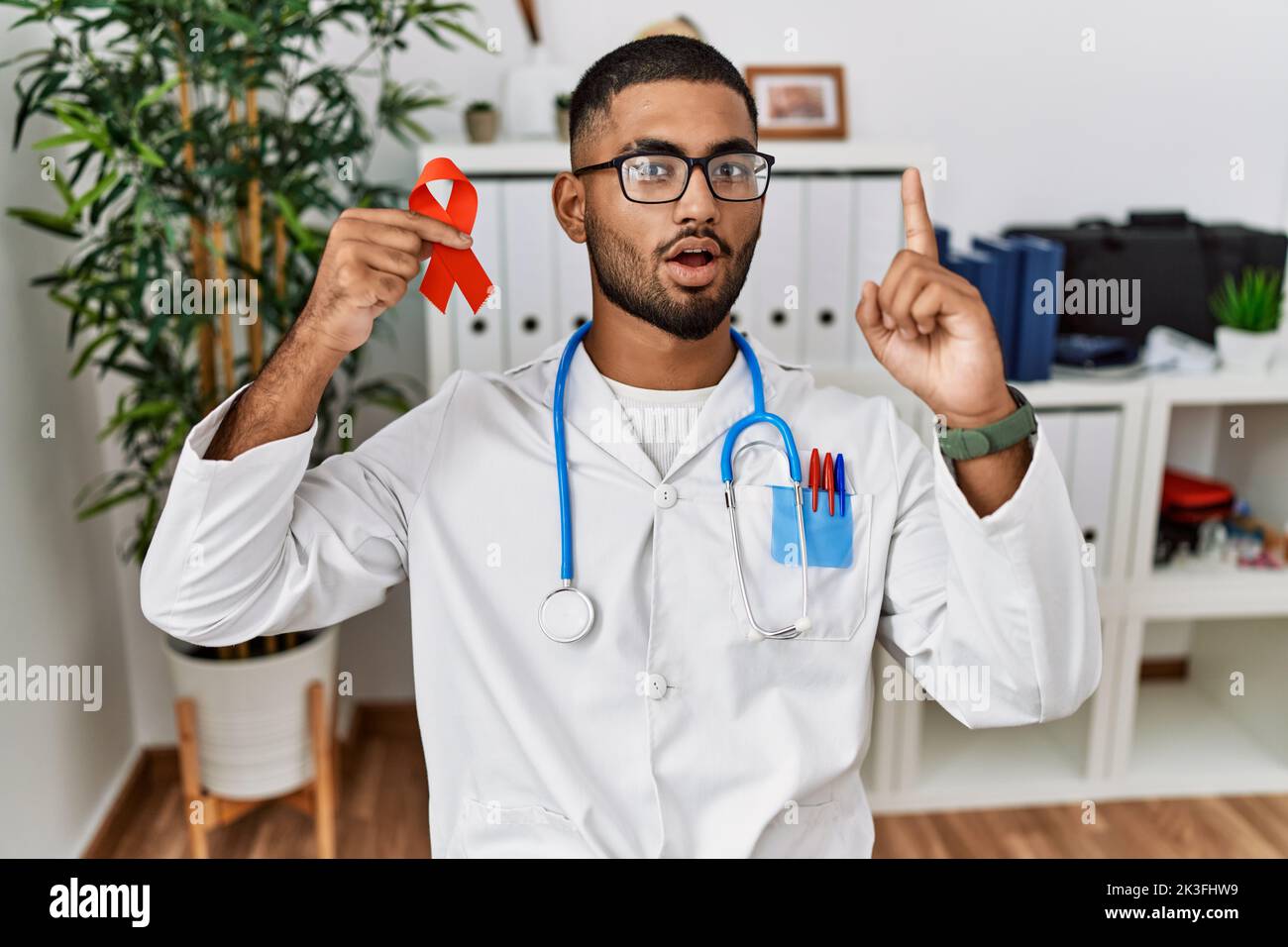 Young indian doctor holding support red ribbon surprised with an idea ...