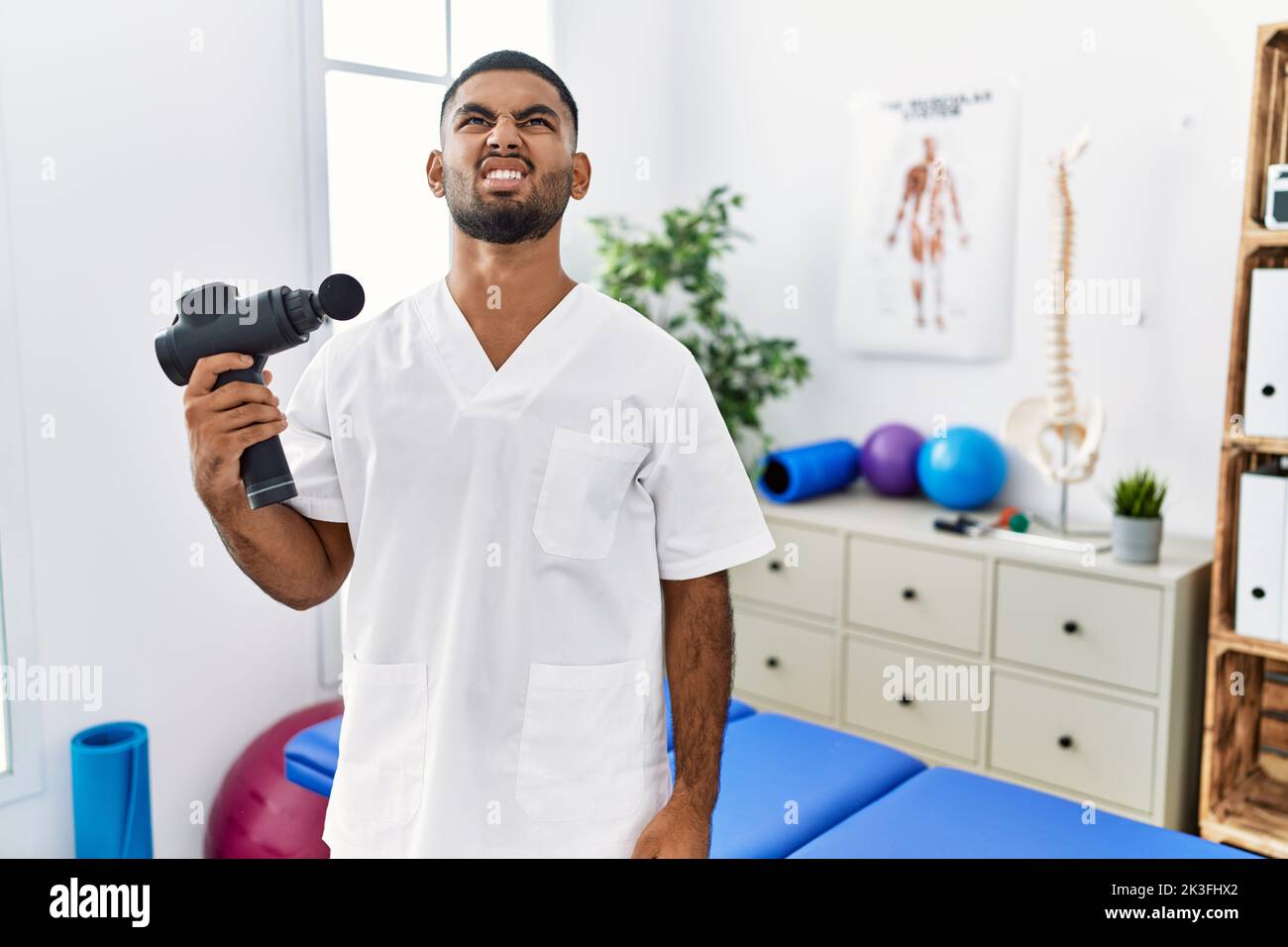 Young indian physiotherapist holding therapy massage gun at wellness ...