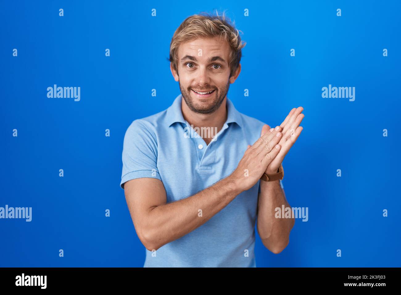 Caucasian man standing over blue background clapping and applauding ...