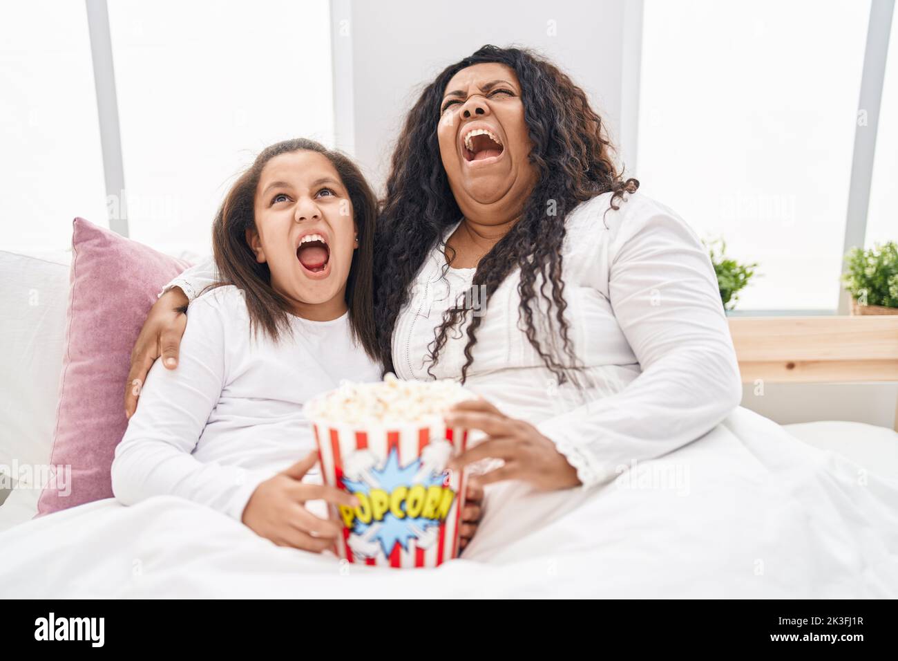 Mother and young daughter eating popcorn in the bed angry and mad ...