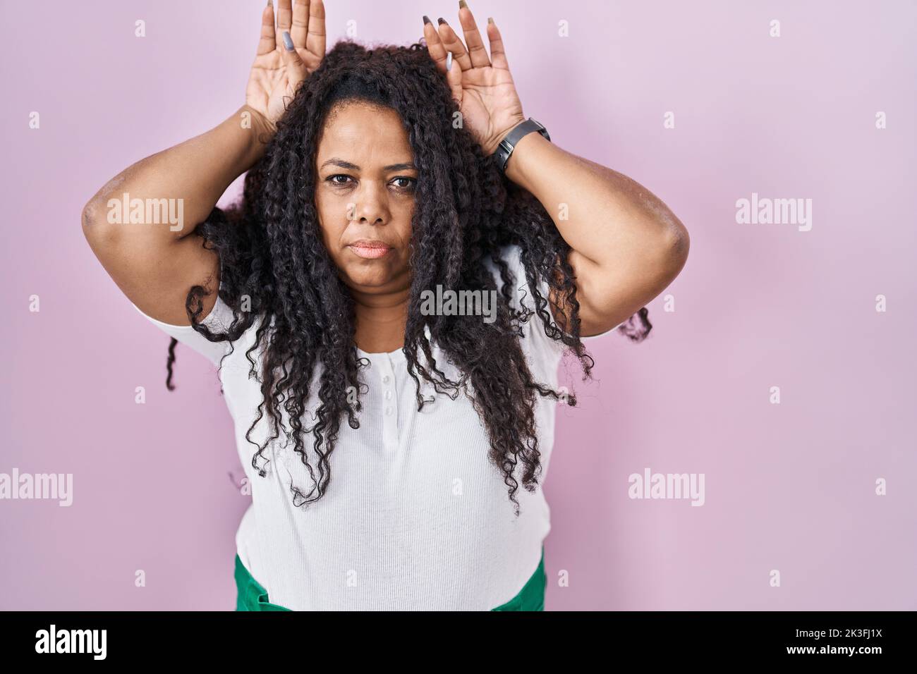 Plus size hispanic woman standing over pink background doing bunny ears ...