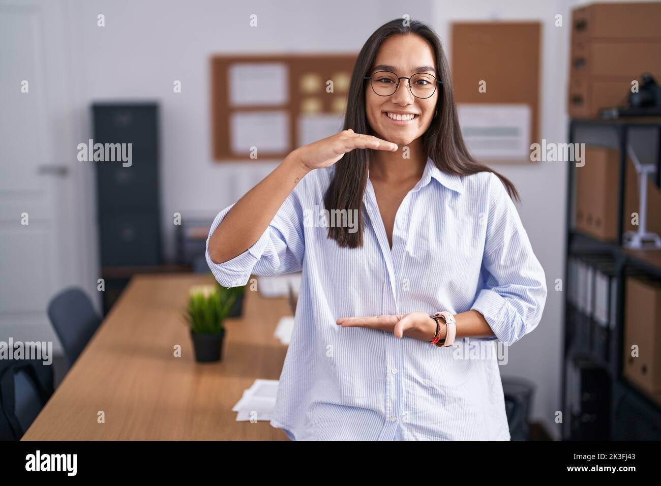 Young hispanic woman at the office gesturing with hands showing big and ...