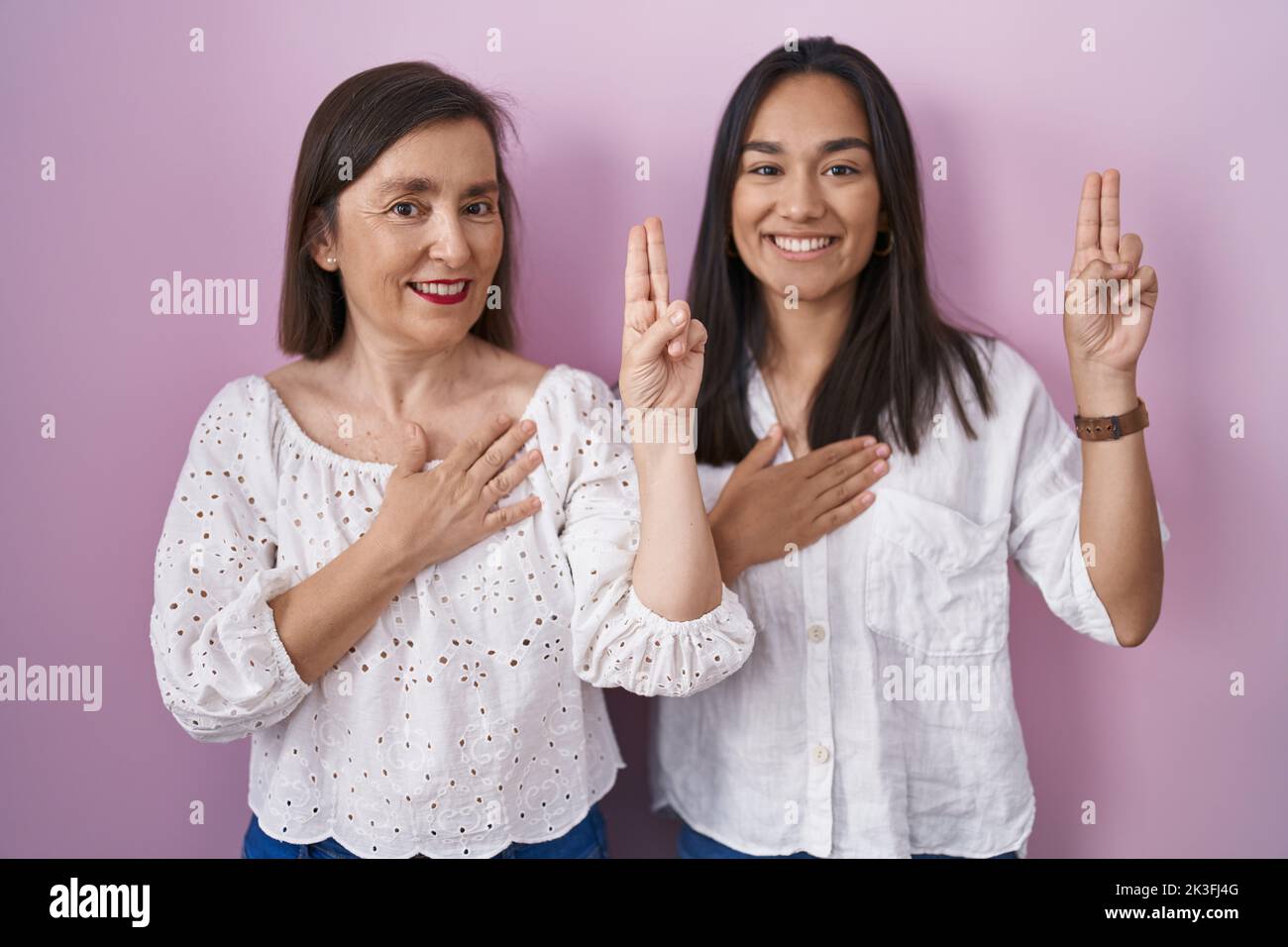 Hispanic mother and daughter together smiling swearing with hand on ...