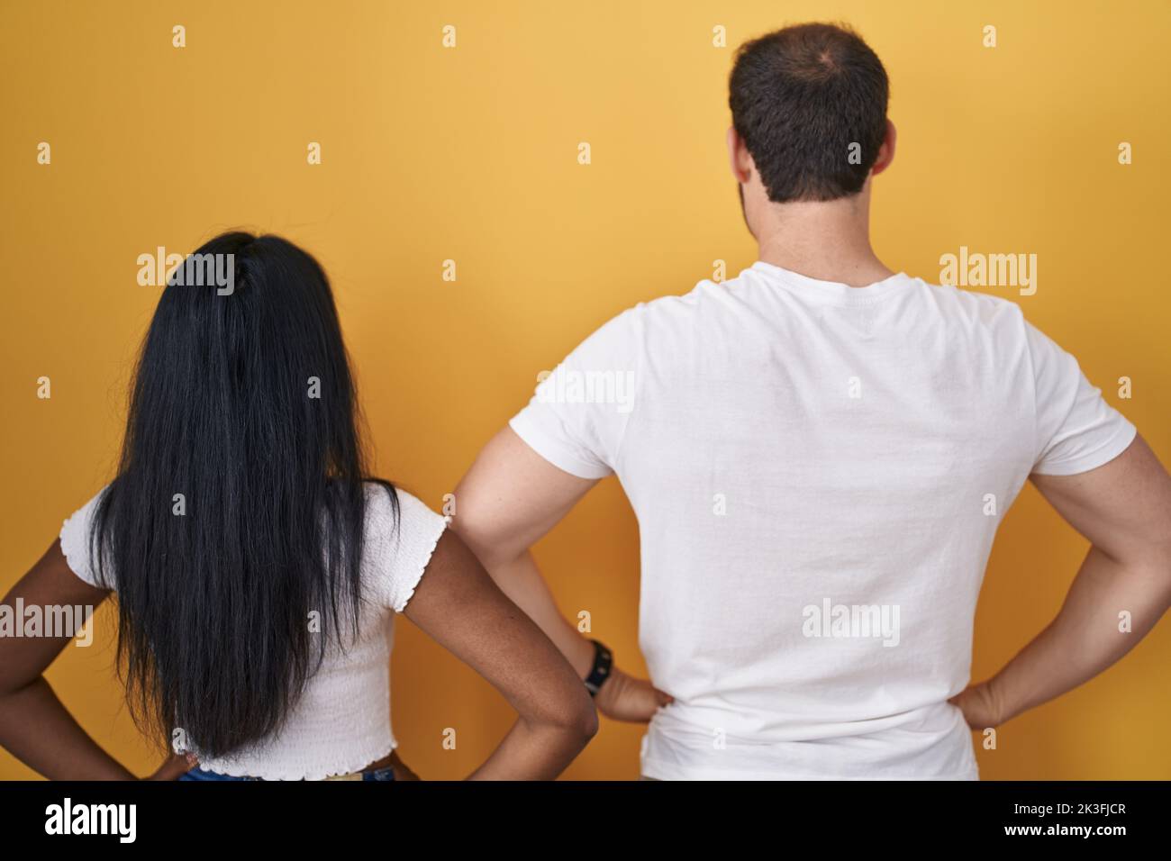 Interracial couple standing over yellow background standing backwards ...