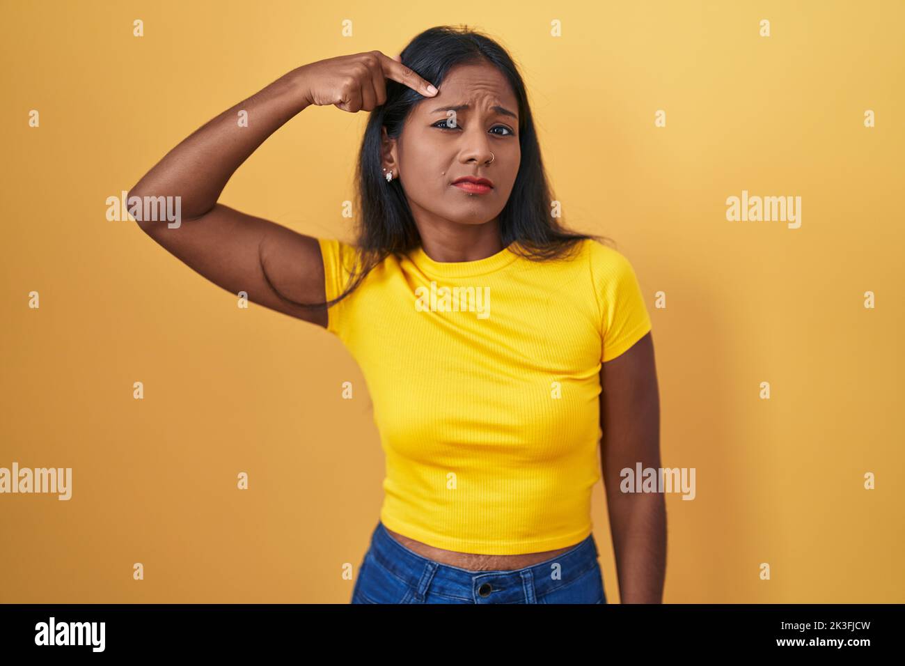 Young indian woman standing over yellow background pointing unhappy to ...