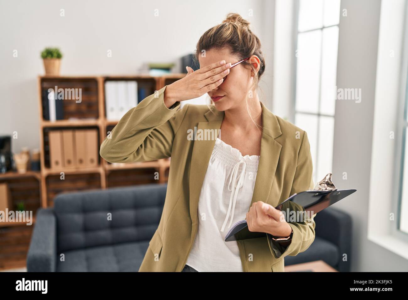 Young woman working at consultation office covering eyes with hand ...