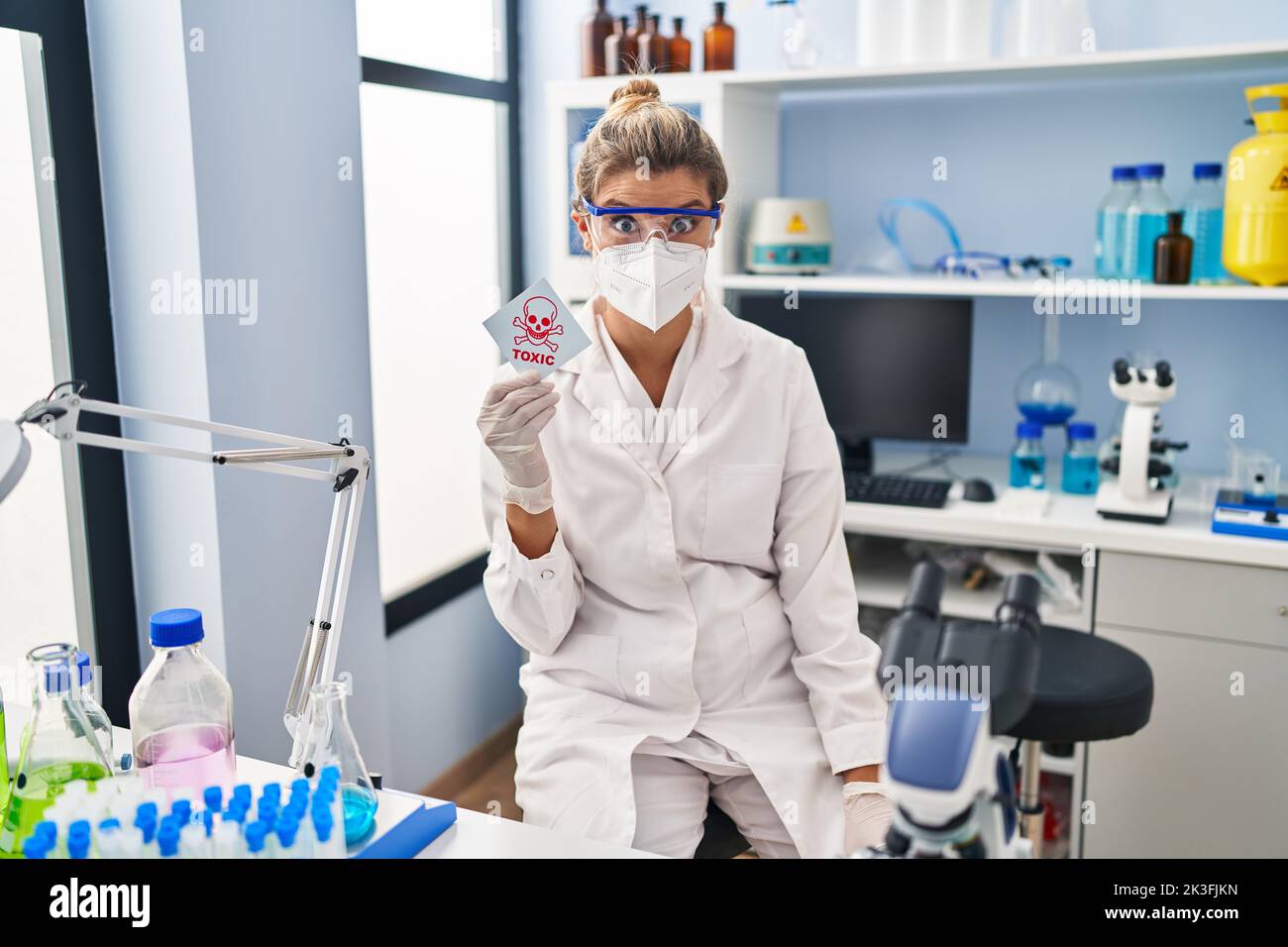 Young woman working at scientist laboratory holding toxic banner scared ...