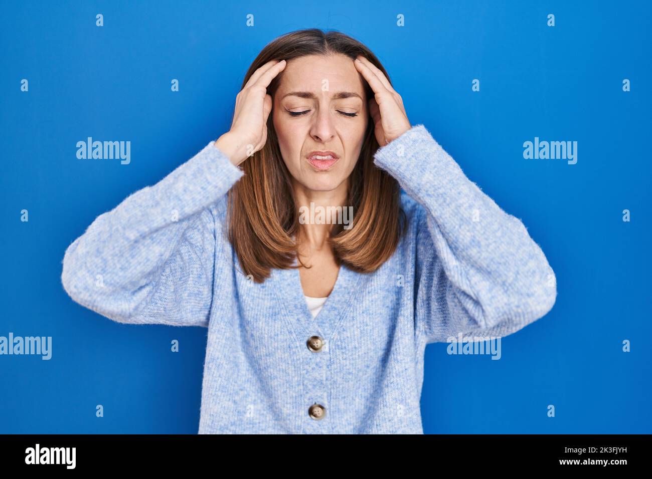 Young woman standing over blue background with hand on head, headache ...
