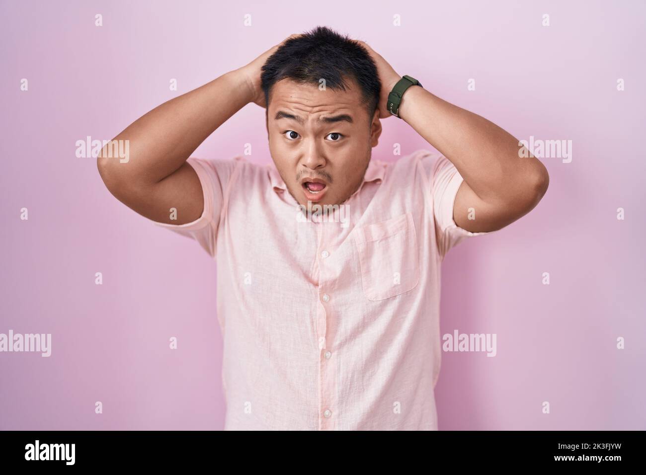 Chinese young man standing over pink background crazy and scared with ...