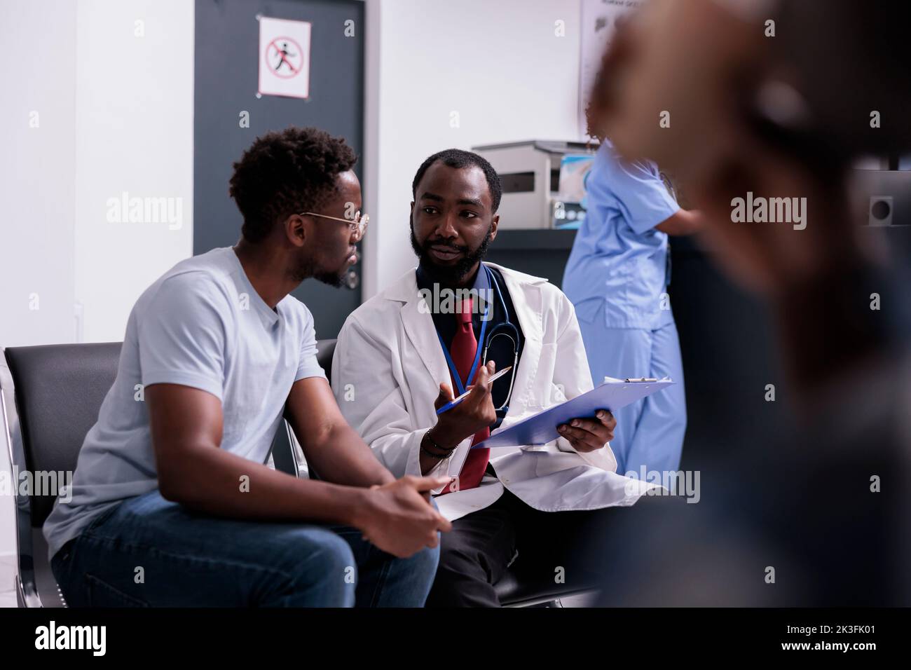 Man talking to general practitioner in waiting room at hopital ...