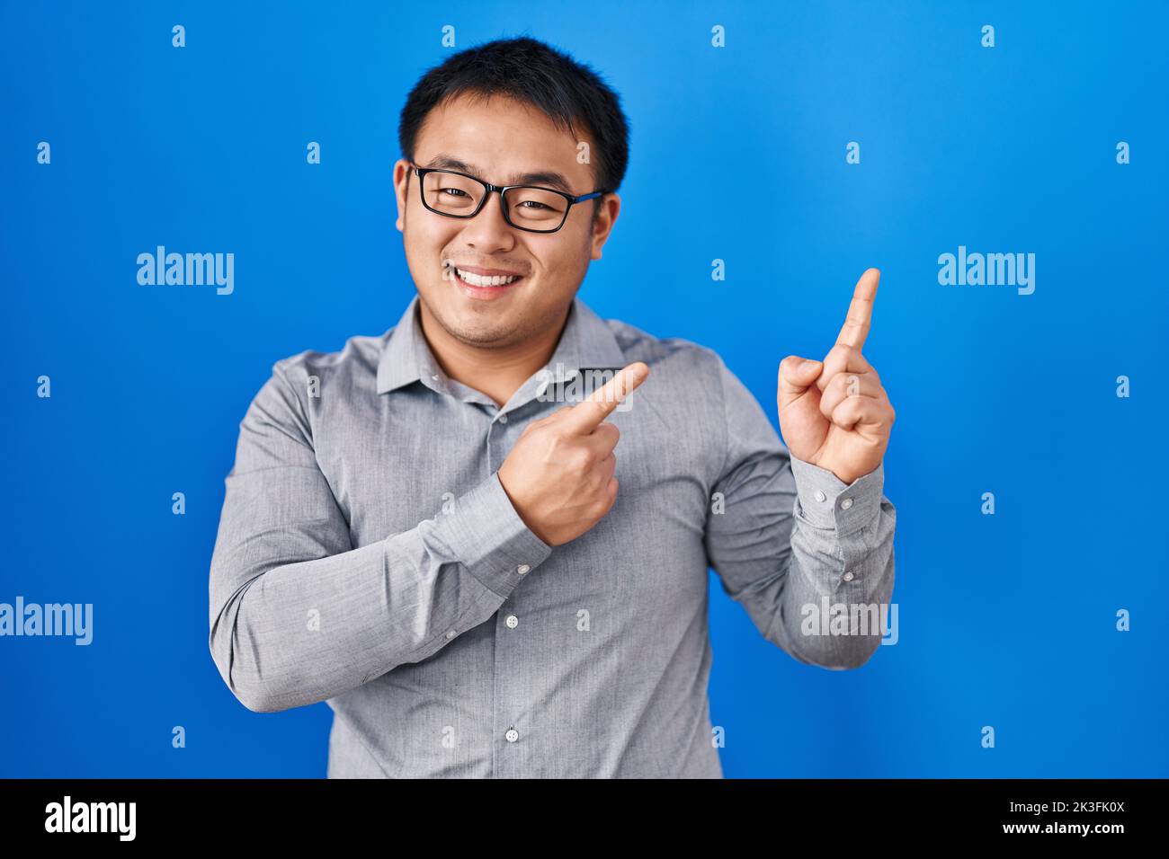 Young chinese man standing over blue background smiling and looking at ...