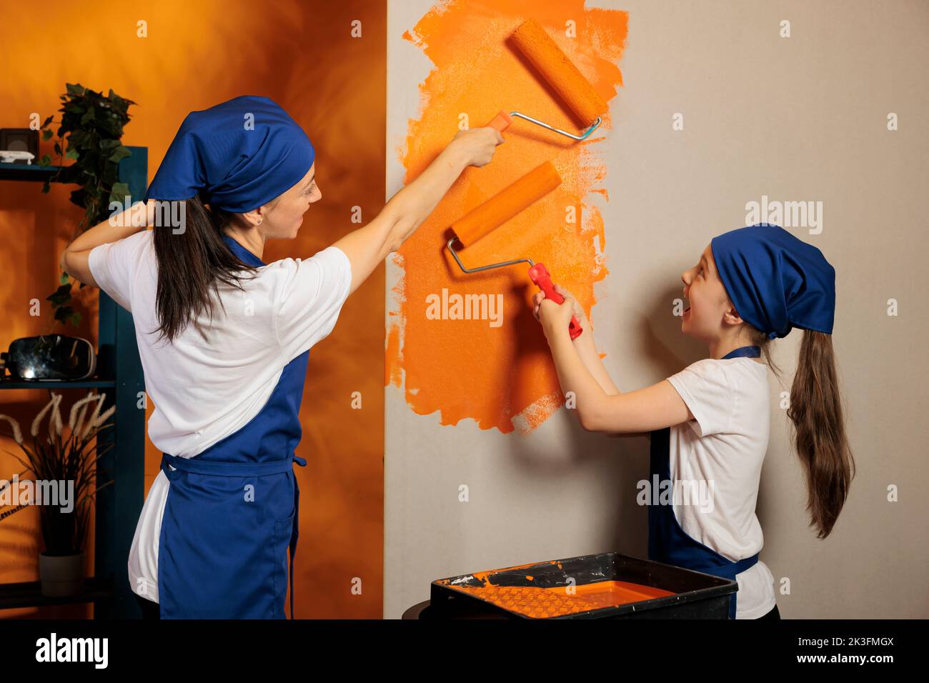 Happy family painting orange walls at home, using roller brush and ...