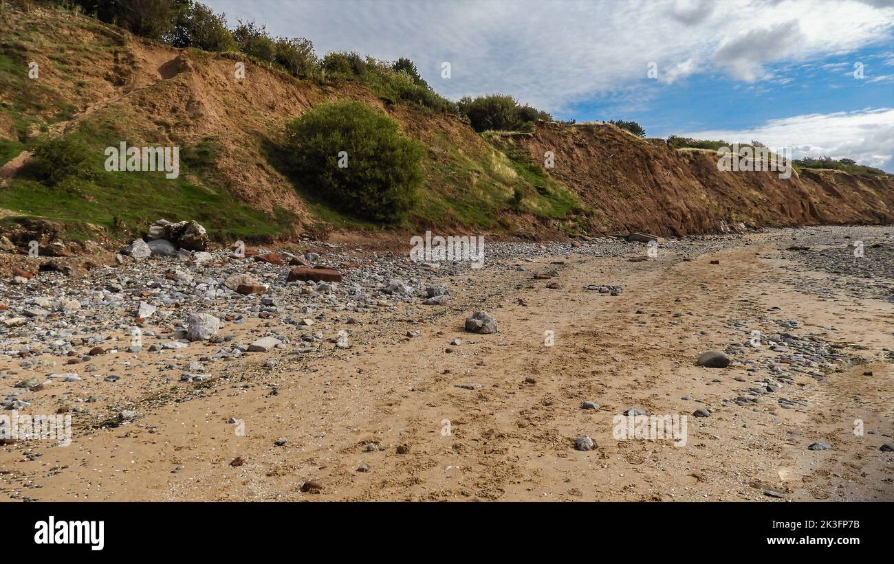 Beach and coastal sand cliffs with a blue cloudy sky and foliage onto ...