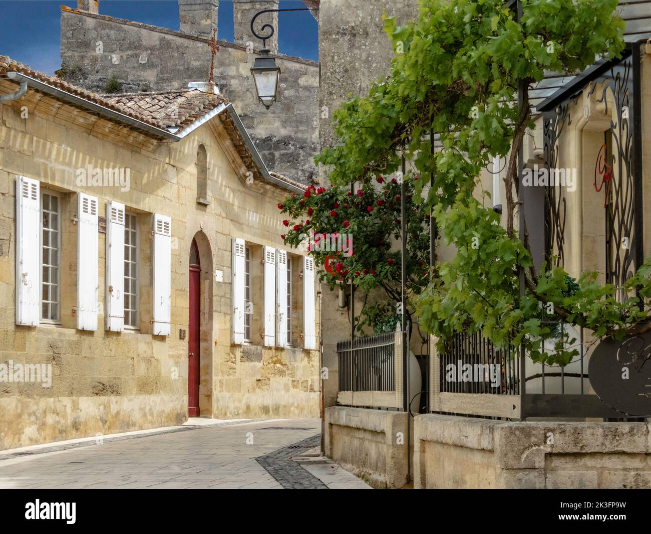 Street with buildings of honey coloured stone a growing vine and red ...