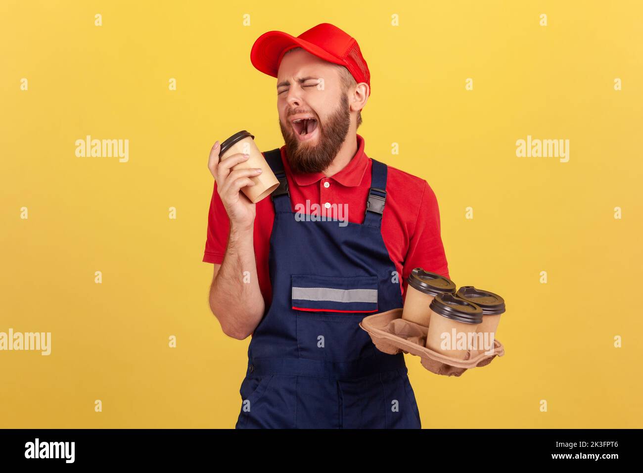 Delivery service. Tired courier man in overalls holding coffee cups and ...