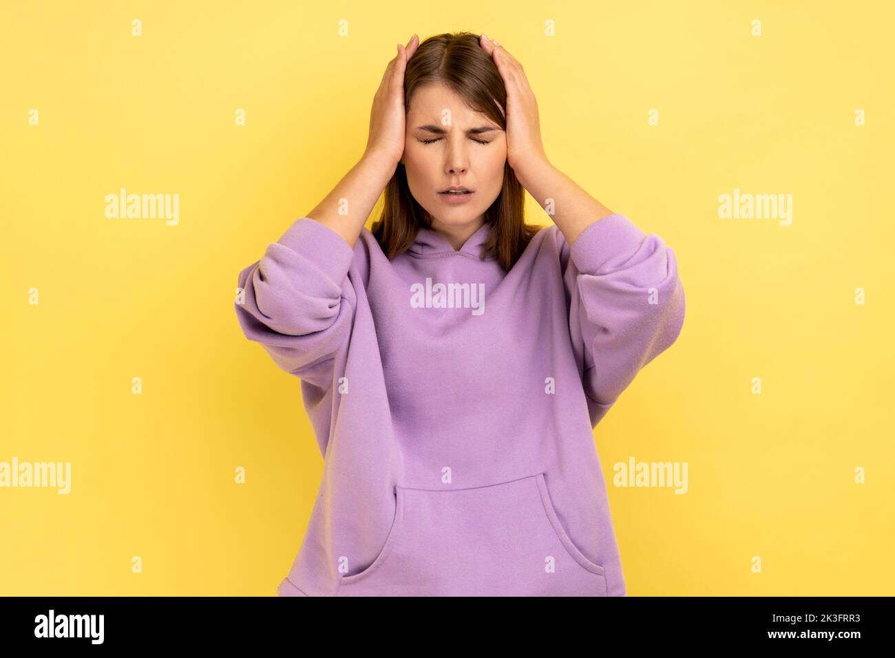 Portrait of ill woman clasping hands over sore head, frowning from ...