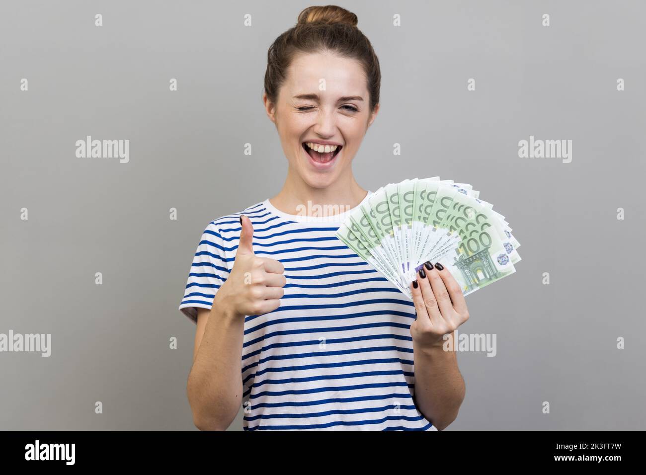 Portrait of woman wearing striped T-shirt holding bunch of euro ...
