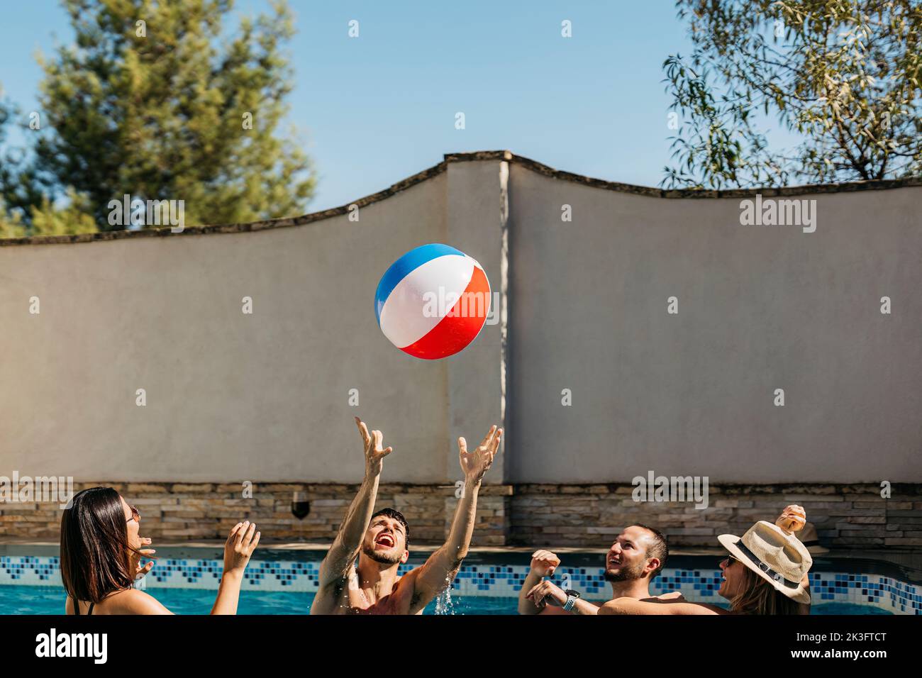 4 friends play in a swimming pool with a ball Stock Photo - Alamy