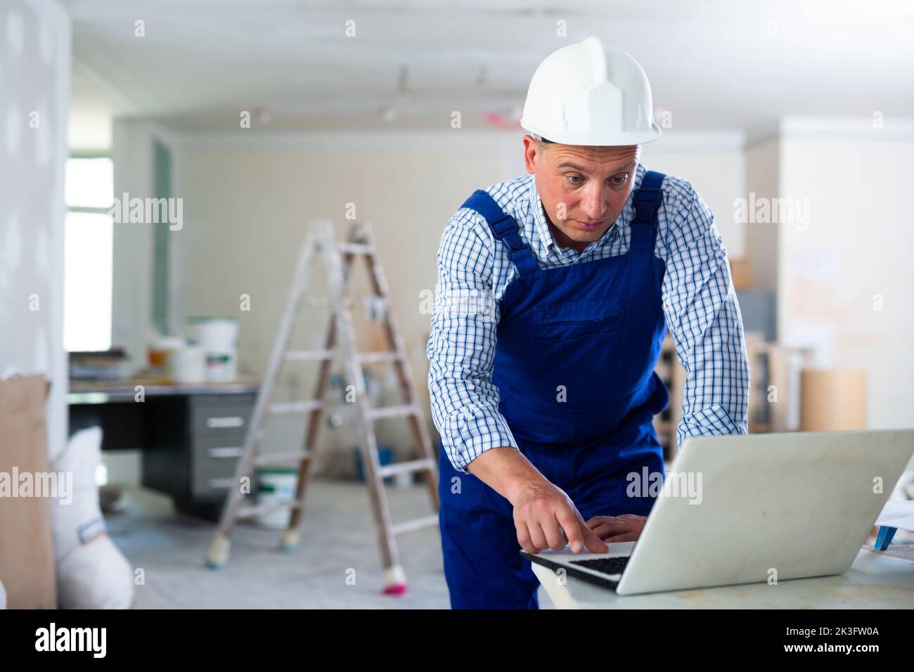 Builder handyman checking plan of house renovation on laptop Stock ...