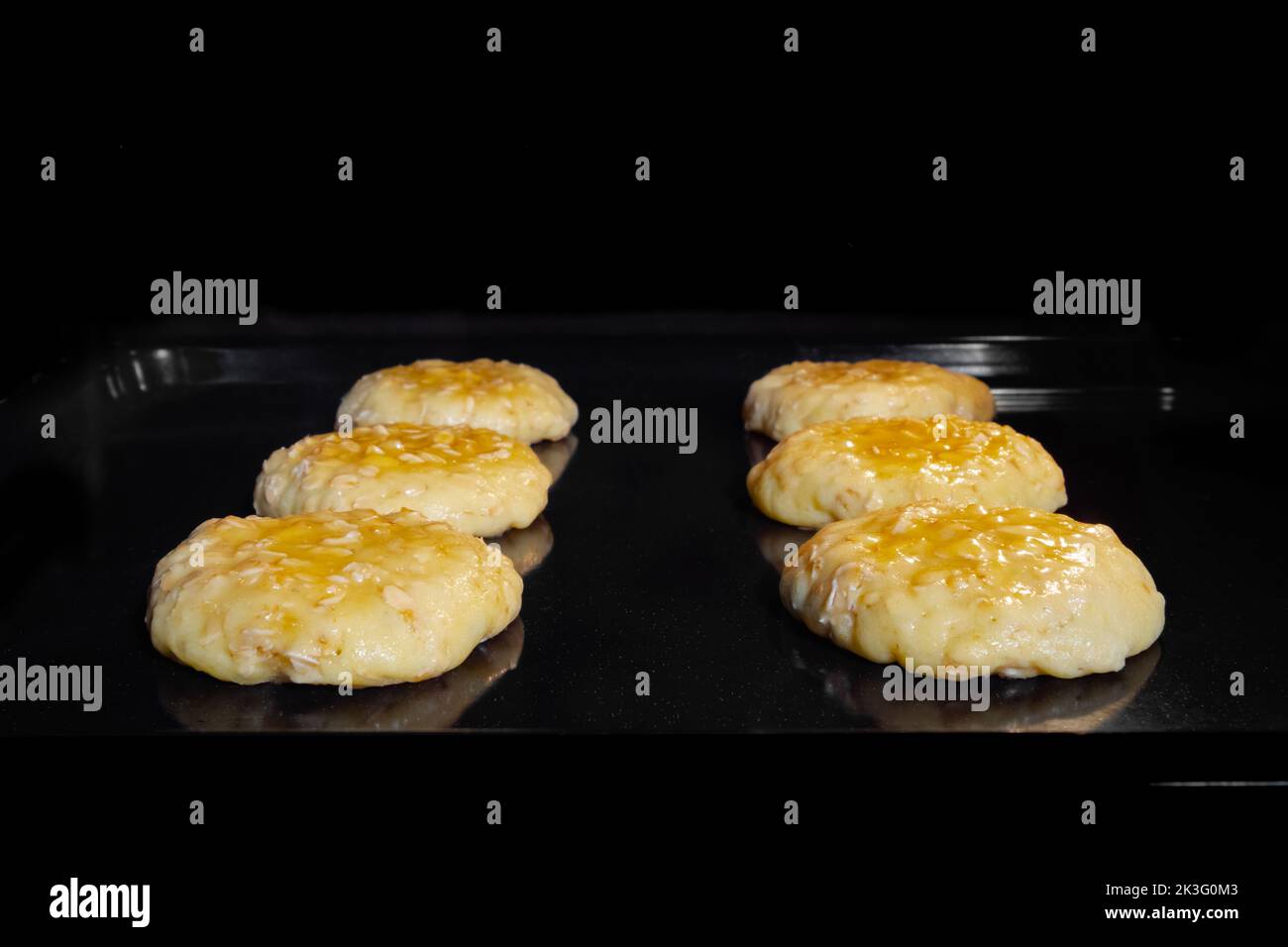 Front view: cooking six crunchy oatmeal cookies on metal sheet in oven ...