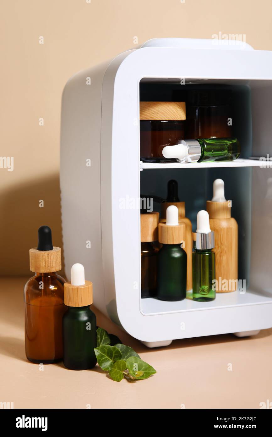 Small refrigerator with natural cosmetics and plant leaves on beige ...