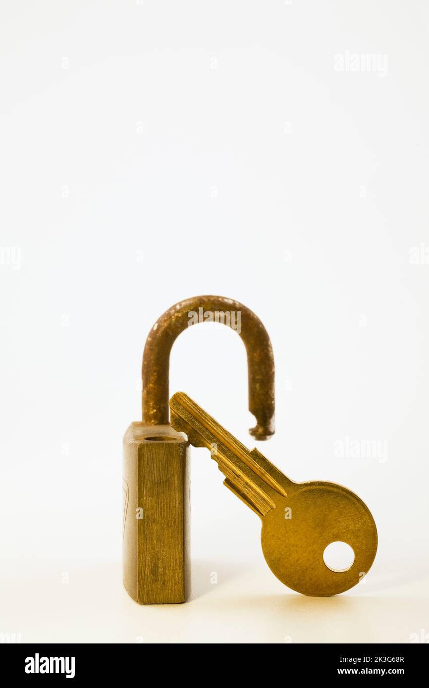 Close-up of brass key leaning against unlocked padlock on white ...