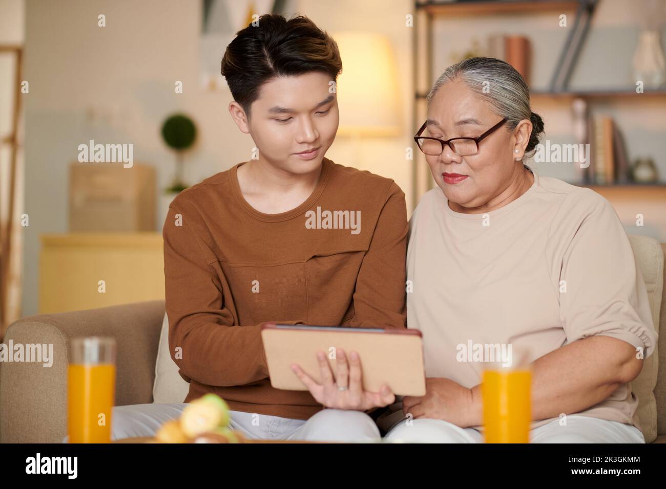 Smiling young man showing grandmother how to use application on digital ...
