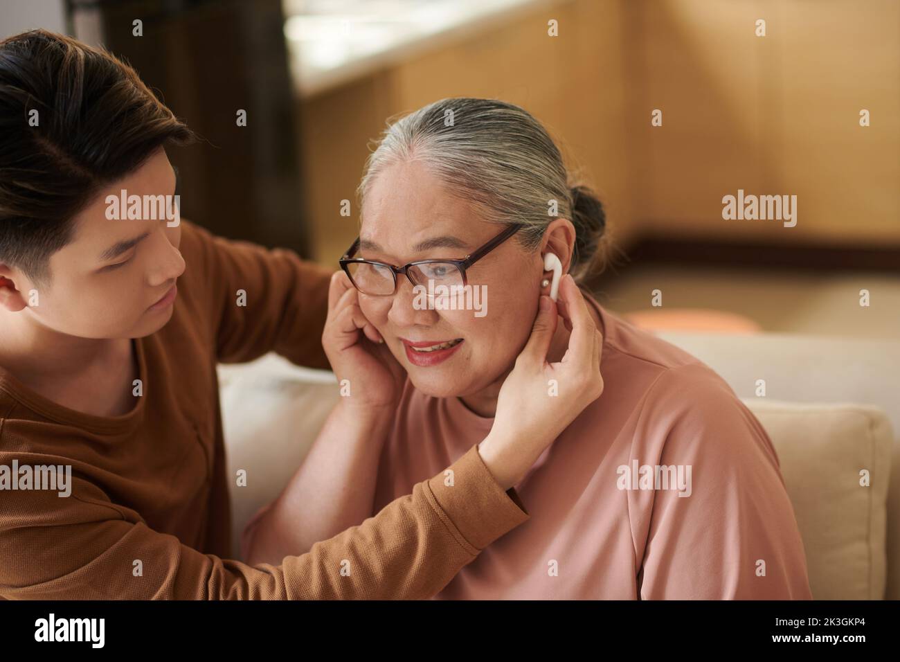 Teenage boy helping smiling grandmother to put in earbuds Stock Photo ...