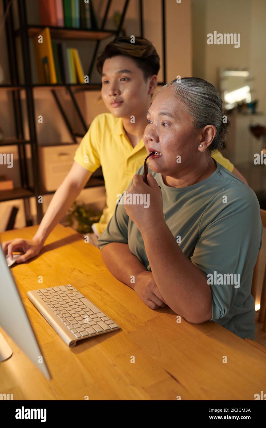 Pensive senior woman biting glasses frame when reading article on ...