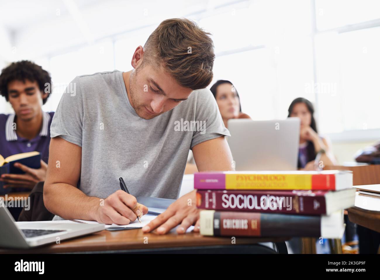 Sure of study success. A handsome young student sitting at a desk with ...