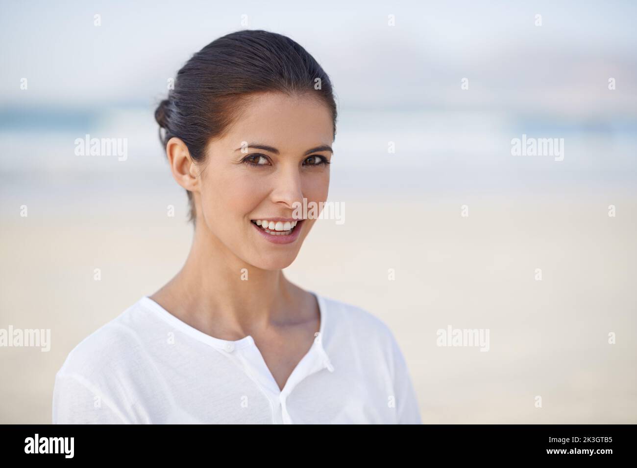 Seaside beauty. A beautiful woman standing on the beach smiling at the ...
