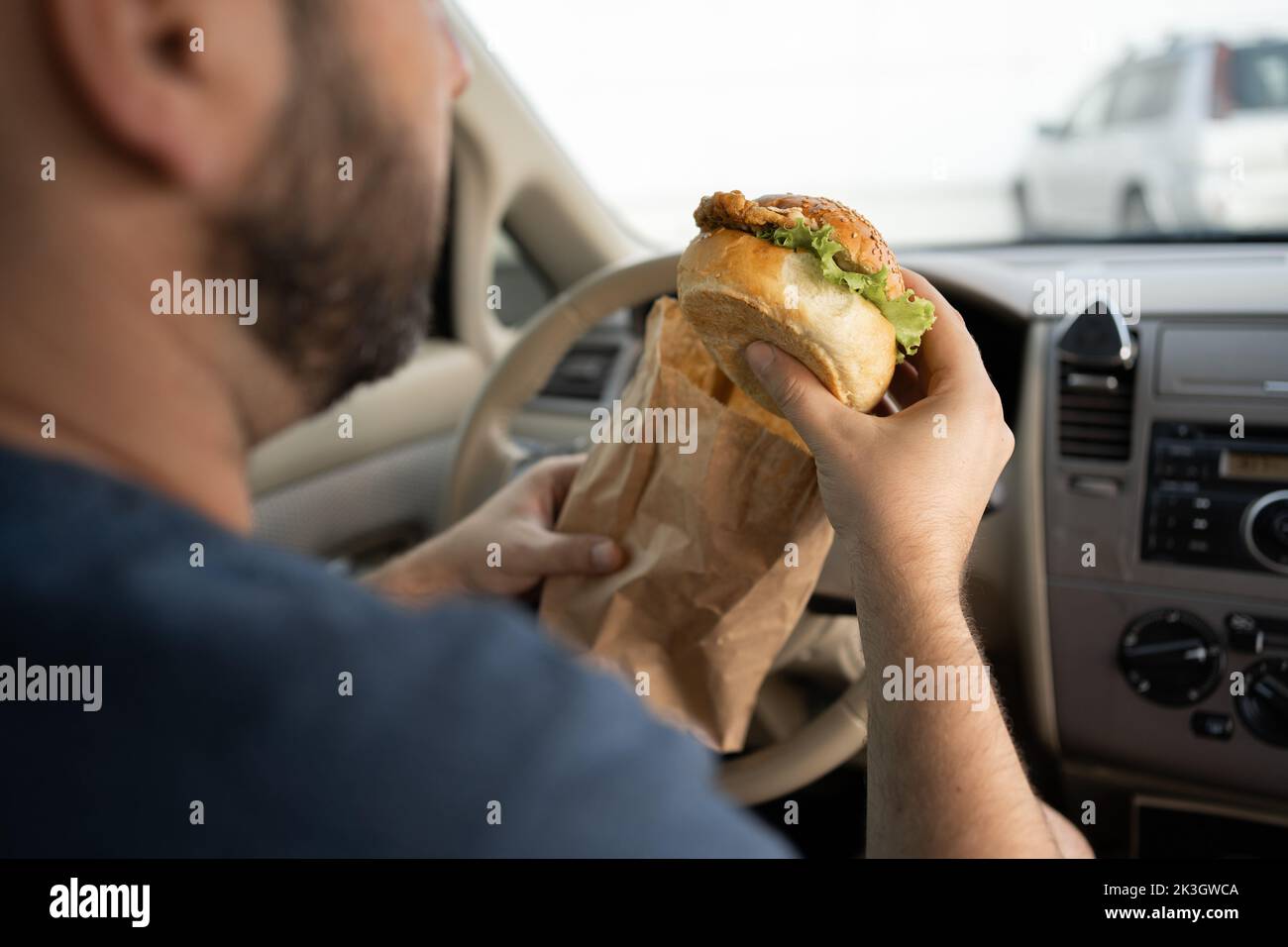 The driver eating a hamburger in the car. Breakfast burger in a traffic ...