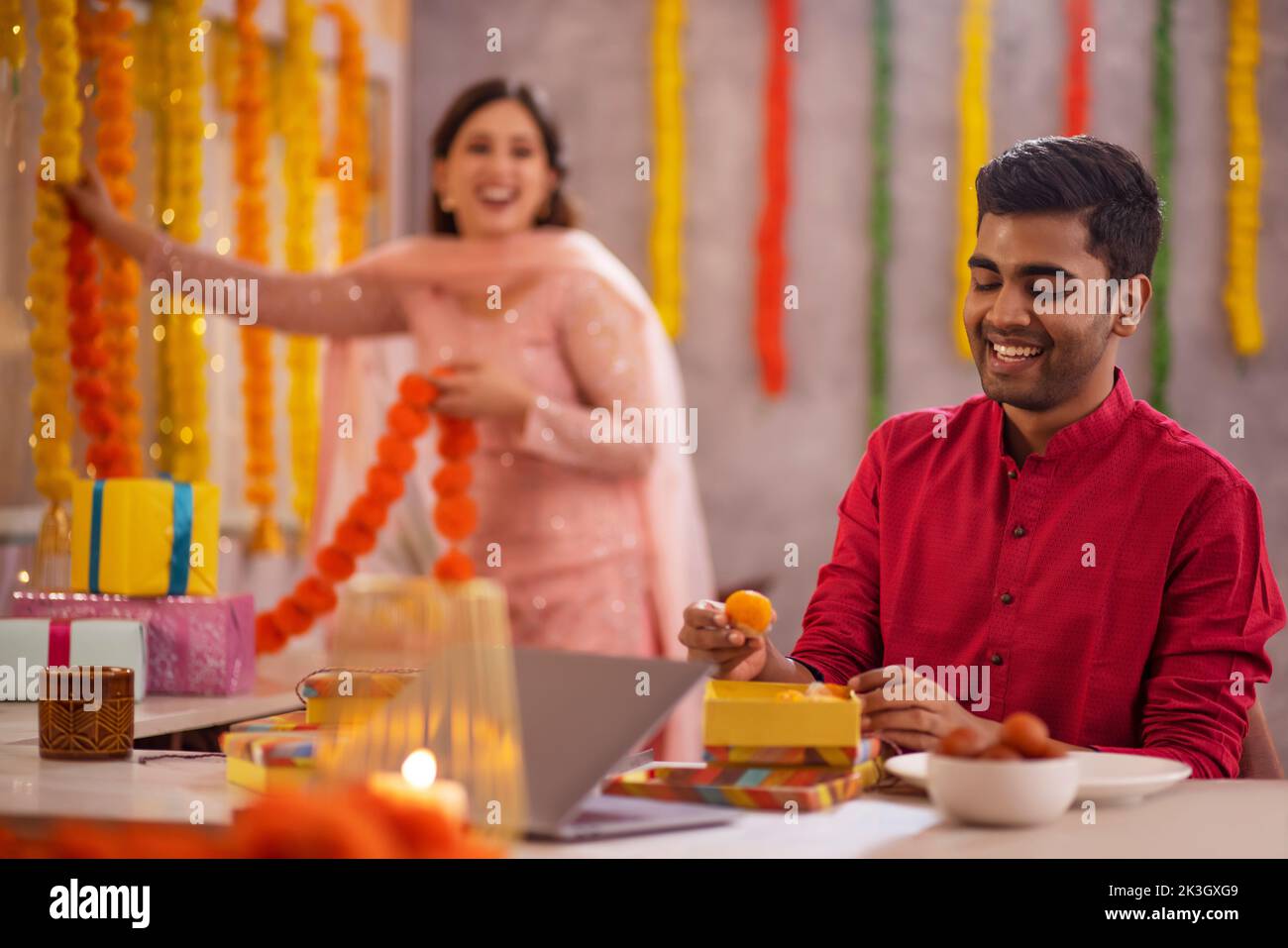 Young man arranging ladoos in sweet box and his female colleague ...