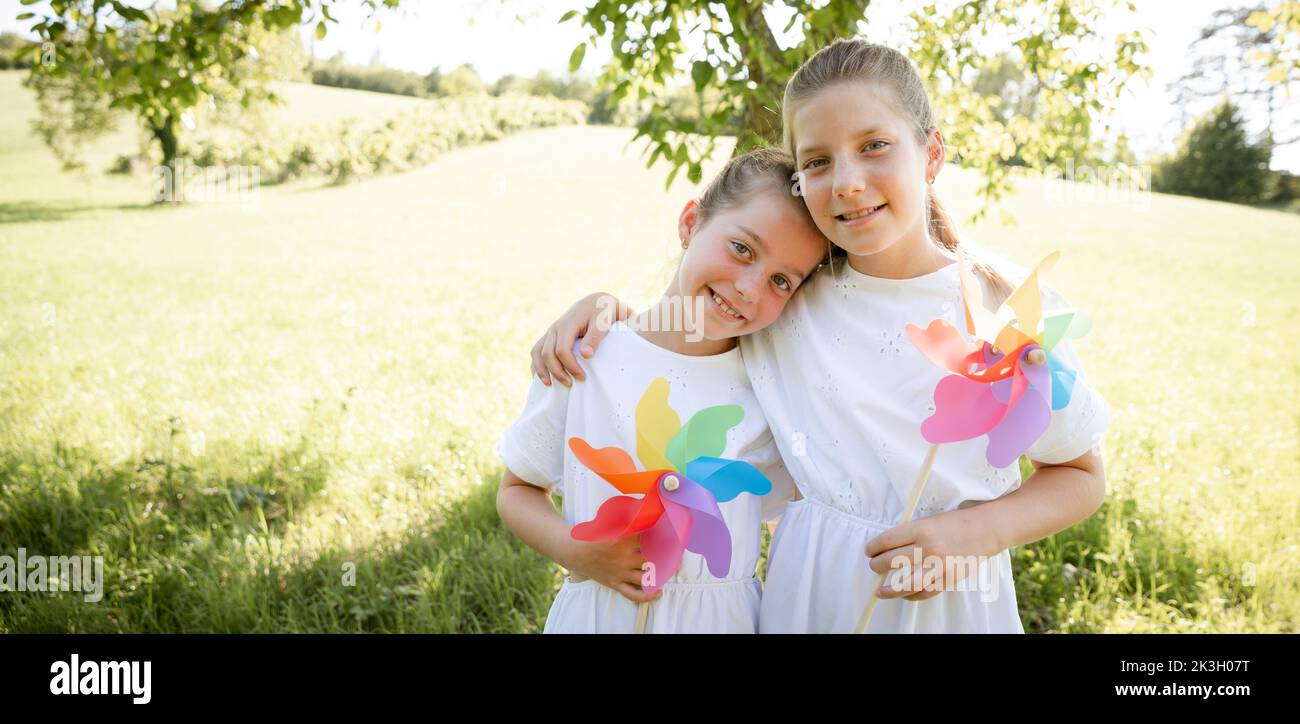 two pretty girls, sisters with white dresses holding colorful pinwheels ...