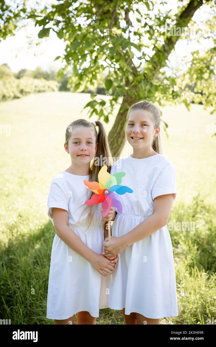 two pretty girls, sisters with white dresses holding colorful pinwheels ...