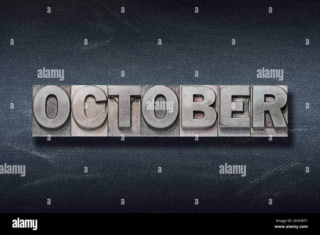 October word made from metallic letterpress on dark jeans background ...