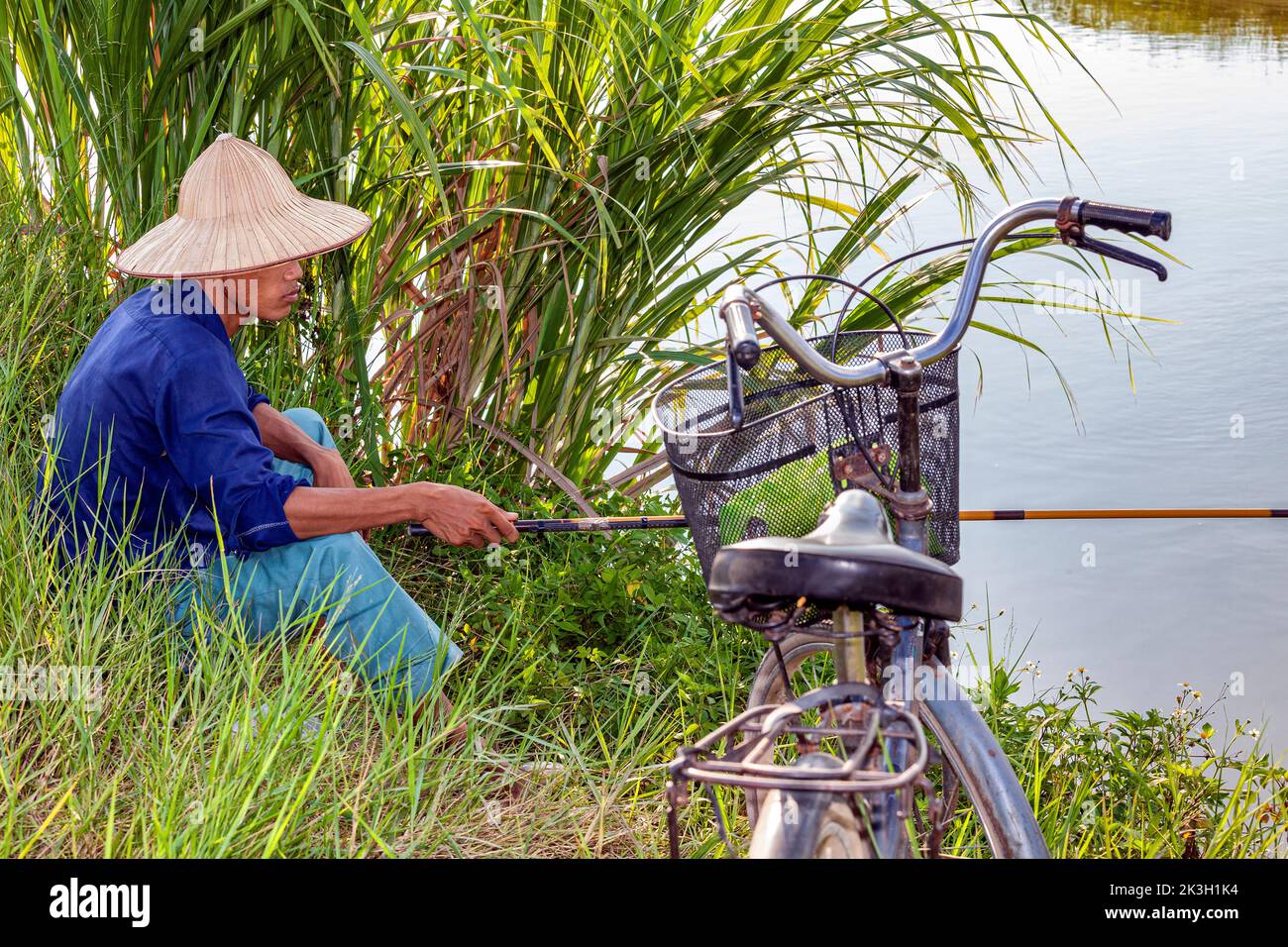 Vietnamese farmer wearing bamboo hat with bicycle and fishing rod in ...