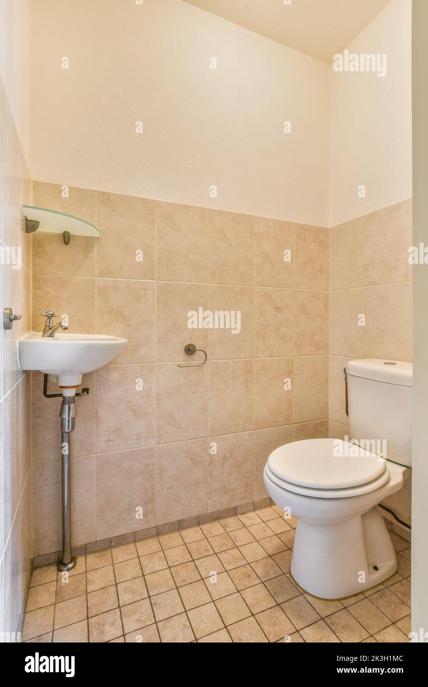 Flush toilet and small sink in corner restroom with beige tile Stock ...