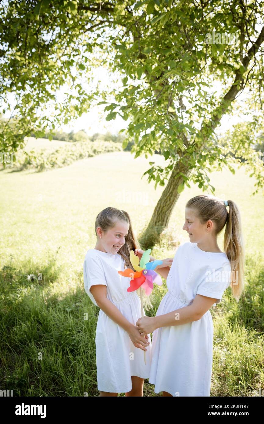 two pretty girls, sisters with white dresses holding colorful pinwheels ...