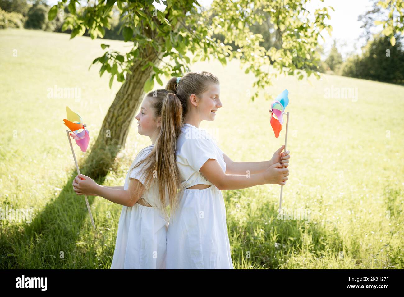 two pretty girls, sisters with white dresses holding colorful pinwheels ...
