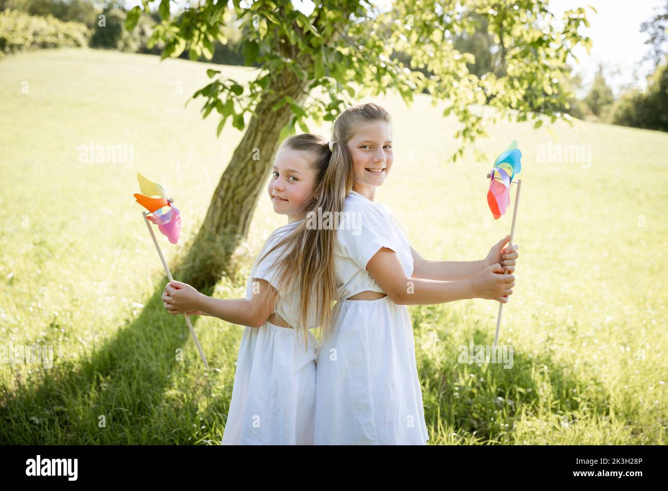 two pretty girls, sisters with white dresses holding colorful pinwheels ...