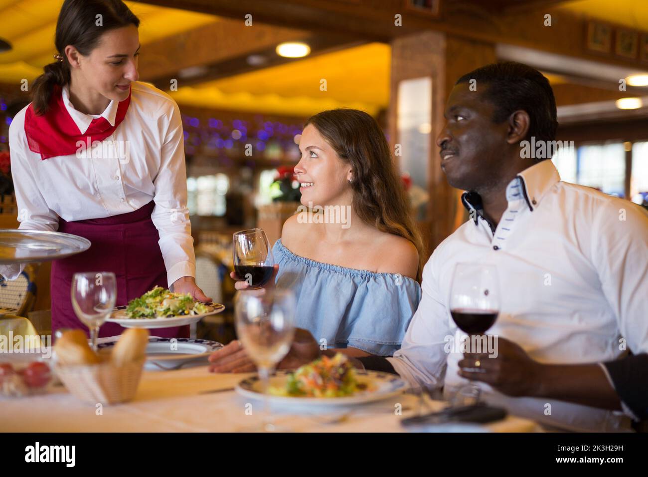 Positive female waiter writing down order from visitors in restaurant ...
