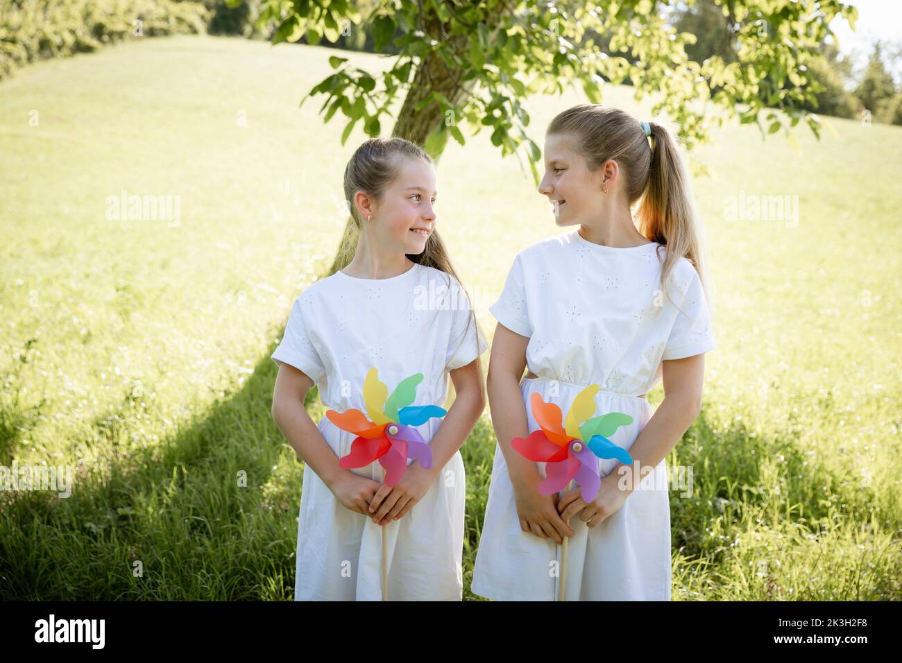 two pretty girls, sisters with white dresses holding colorful pinwheels ...