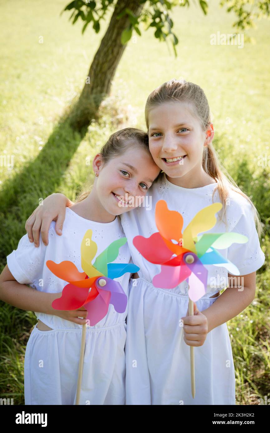 two pretty girls, sisters with white dresses holding colorful pinwheels ...