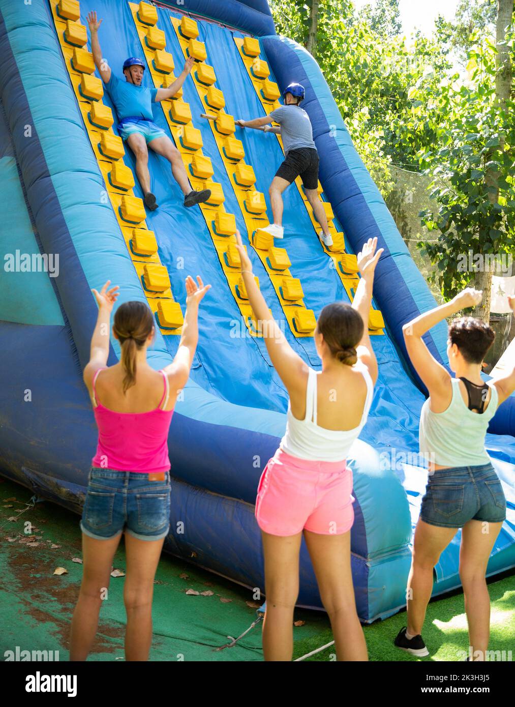 Cheerful man sliding down inflatable slide in outdoor amusement park ...