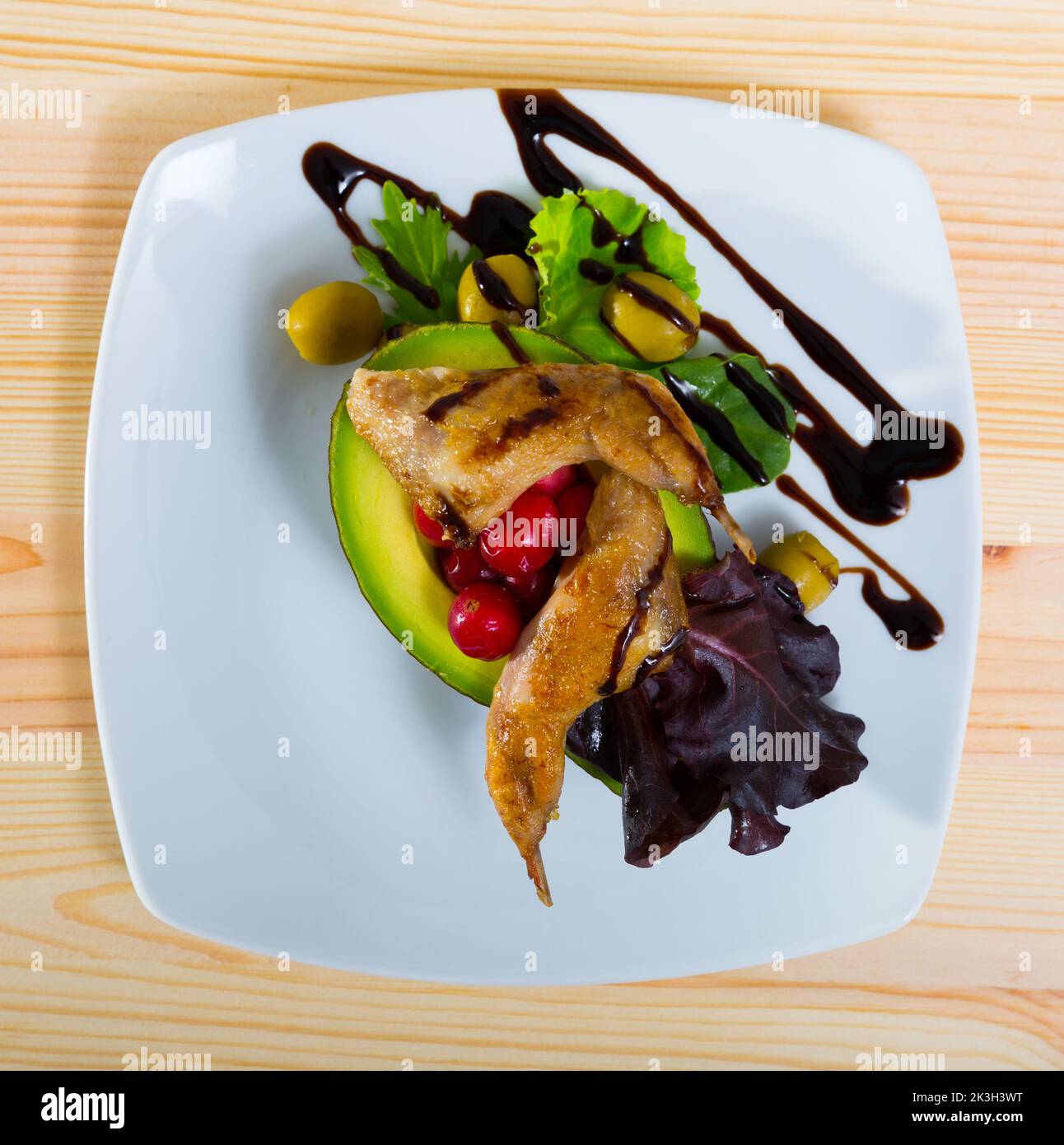 Fried legs of quail served with balsamic pasta and avocado with greens ...