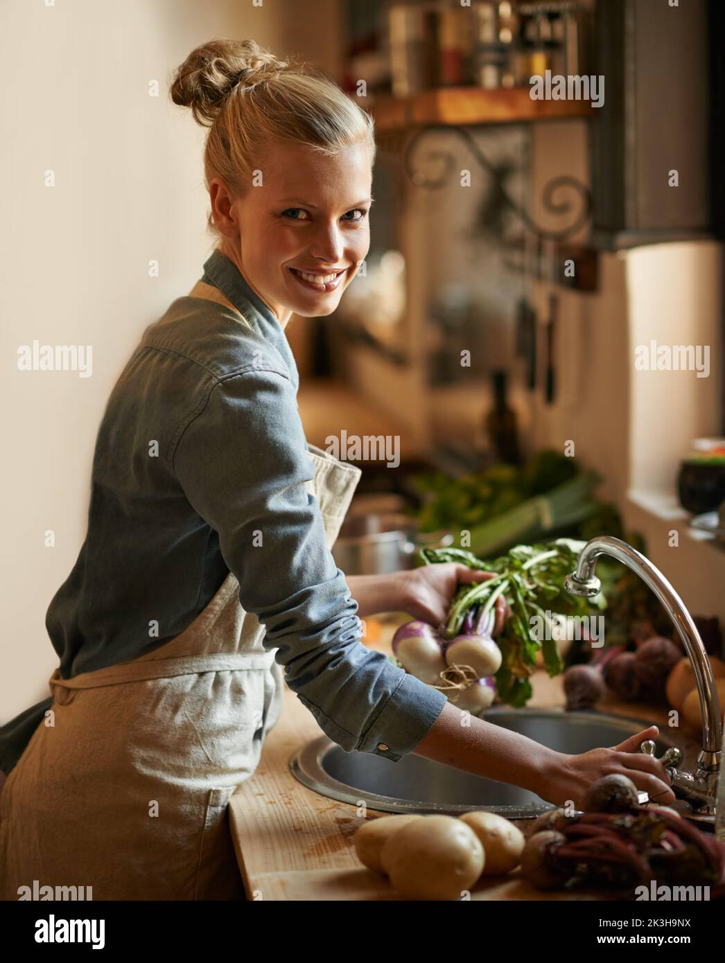 Cooking with love. Portrait of a smiling young woman washing vegetables ...