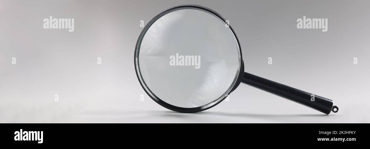 Single magnifying glass with black handle, leaning on grey surface ...