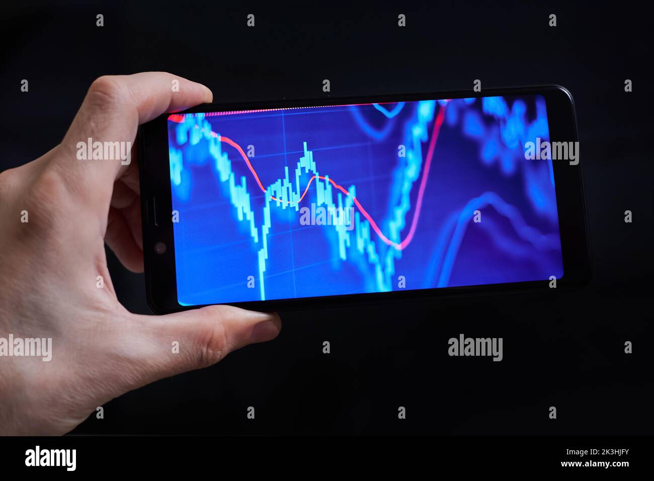 Trader analyzes stock market data in smartphone on dark background ...